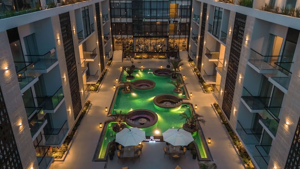 Um átrio moderno de hotel com piscina central, várias varandas e áreas de estar ao ar livre.