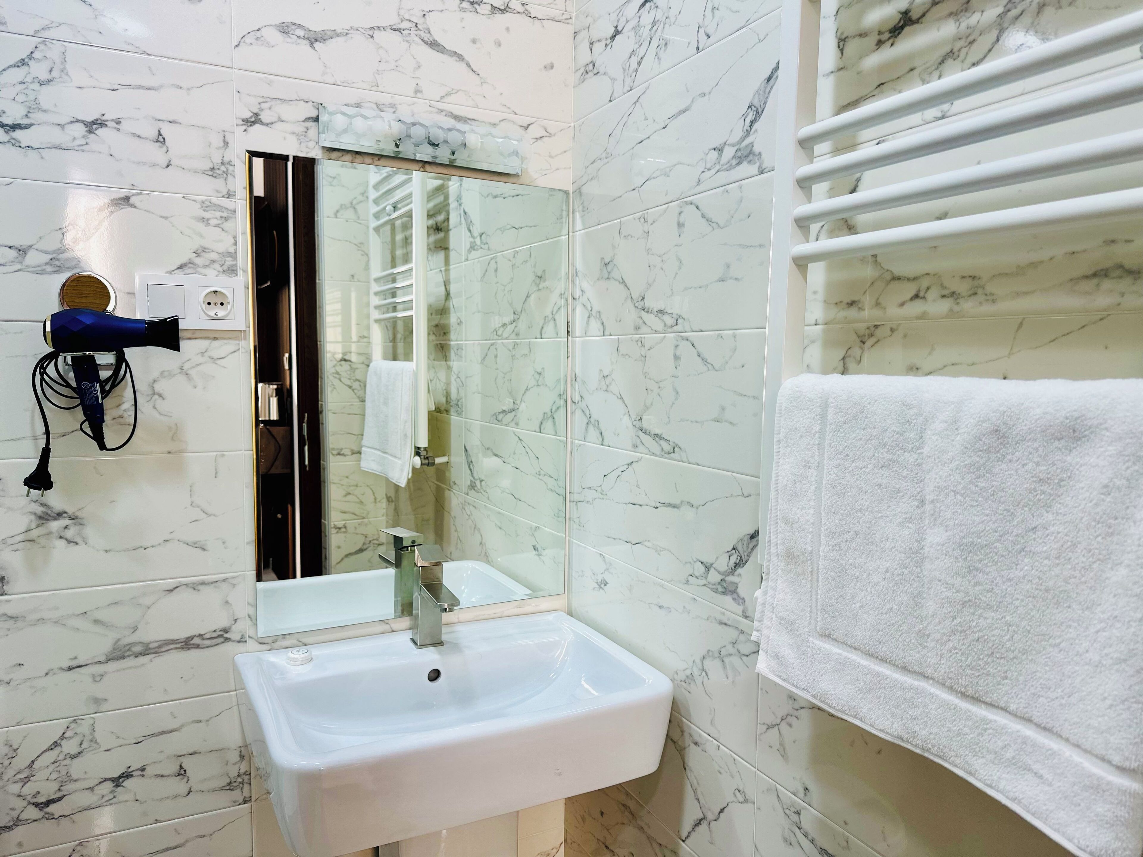 Casa de banho com lavatório branco, azulejos de mármore, espelho e um porta-toalhas.