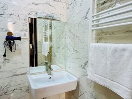 Casa de banho com lavatório branco, azulejos de mármore, espelho e um porta-toalhas.