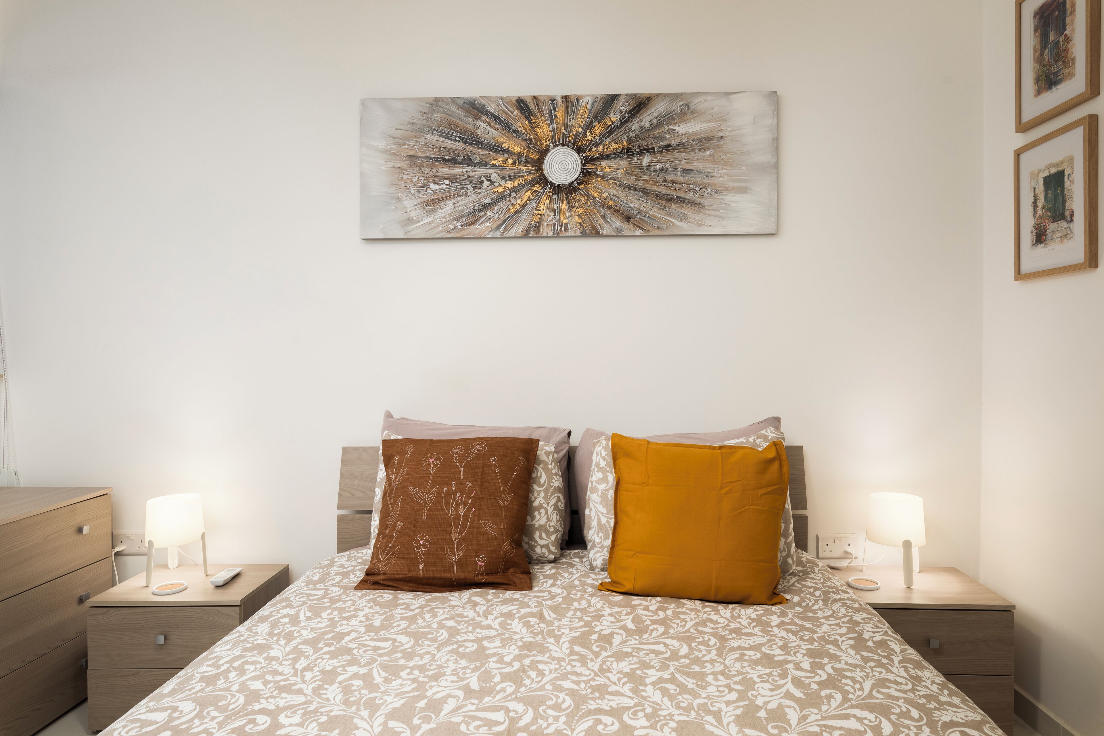 Quarto com uma cama, duas mesas de cabeceira, um criado-mudo, uma obra de arte na parede e um quadro emoldurado.