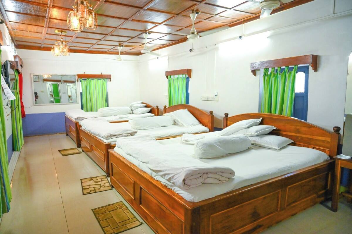 Quarto de hotel com três camas de madeira, cortinas verdes e teto de madeira.