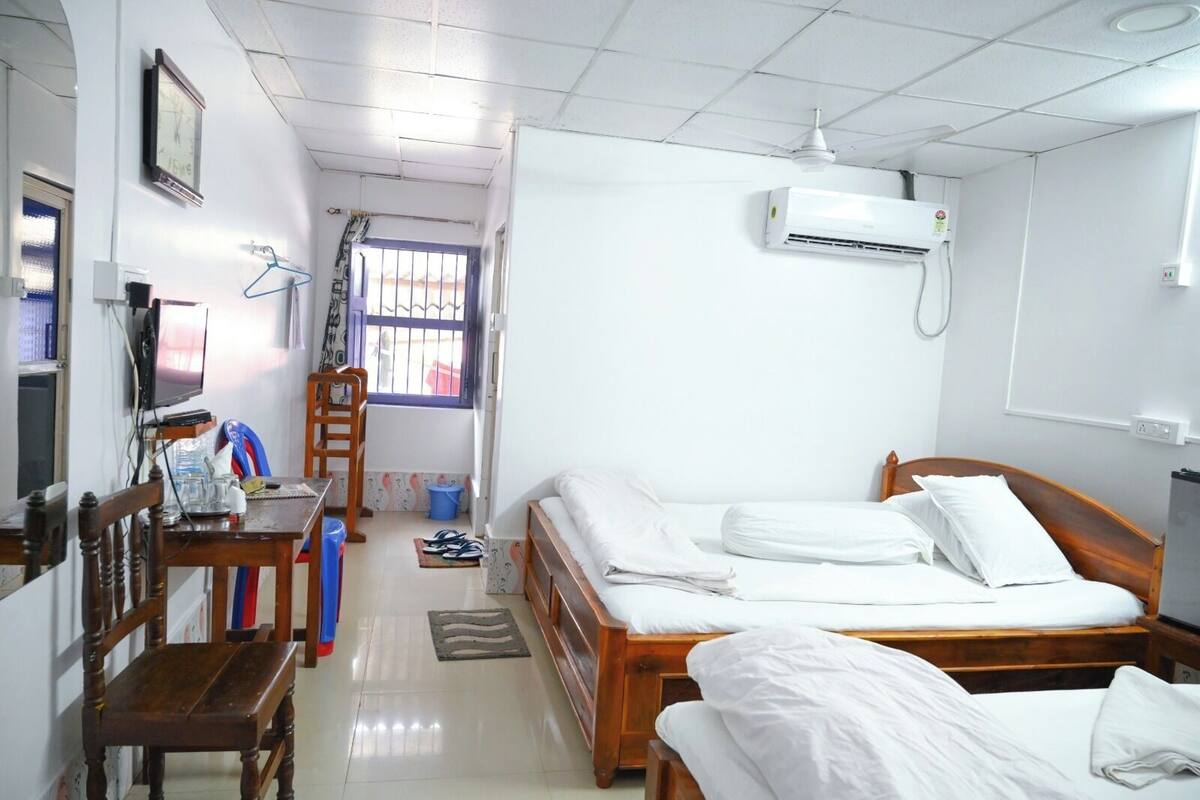 Quarto pequeno e limpo com duas camas de solteiro, uma escrivaninha com cadeira, TV e ar condicionado.
