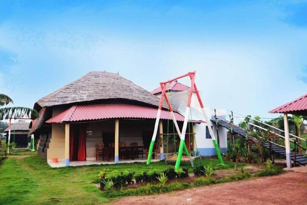 Uma casa tradicional com telhado de palha, varanda com cadeiras e balanço.