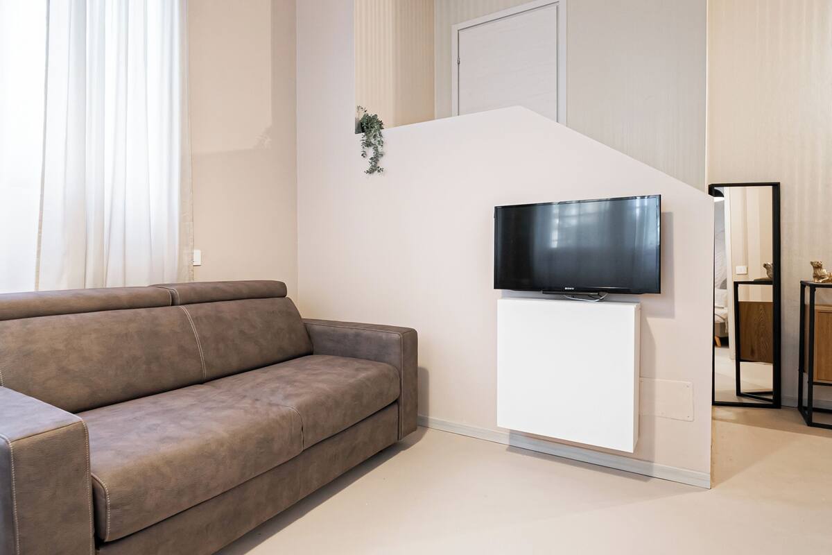 Uma sala de estar moderna com um sofá marrom, um armário branco e uma televisão na parede.