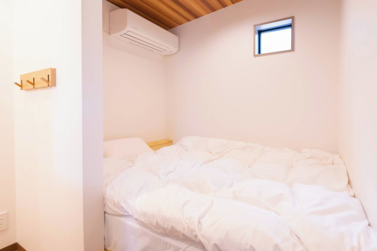 Quarto com cama, ar condicionado, uma pequena janela e uma tomada.