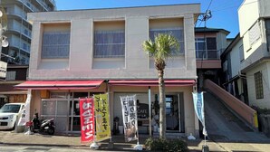 Um edifício de dois andares com toldo vermelho, uma palmeira em frente e várias bandeiras.