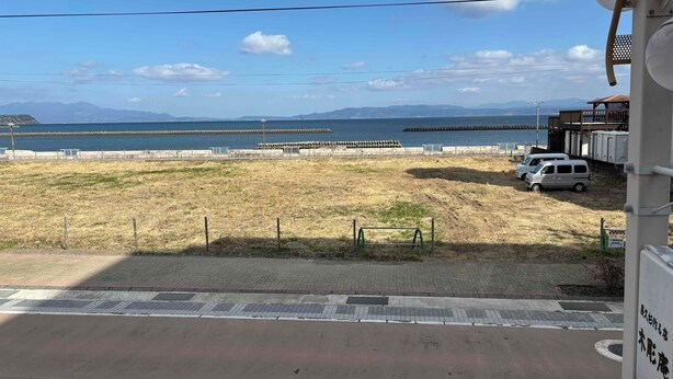 Vista costeira com área gramada, um caminho pavimentado e uma van estacionada.