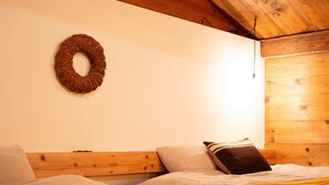 Quarto com vigas de madeira no teto, duas camas com roupa de cama branca e azul, um painel de parede marrom e uma cabeceira de madeira.