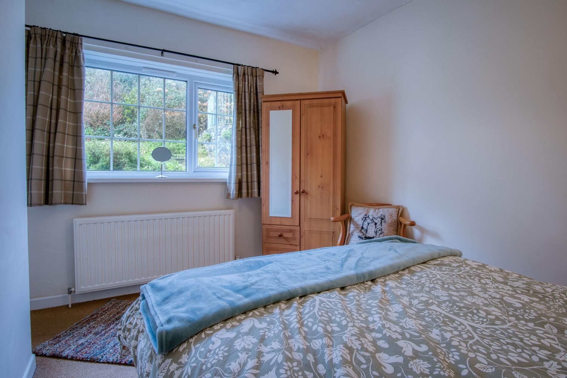 Quarto com cama, guarda-roupa de madeira, cadeira e janela com cortinas.