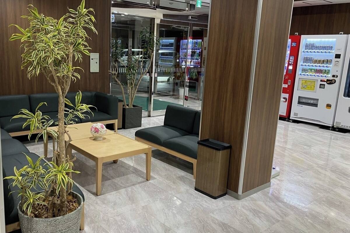 Um lobby moderno com sofás verde escuro, uma mesa de centro de madeira e plantas em vasos.