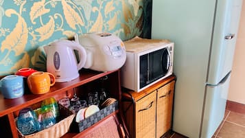 Uma cozinha com micro-ondas, chaleira e cafeteira em uma prateleira, geladeira e cestos de vime com copos.