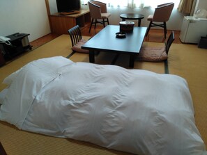 Quarto com cama, mesa, cadeiras, televisão e geladeira.