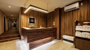 Uma área de recepção de hotel com um balcão de madeira, uma placa com texto em japonês, um laptop e uma pilha de toalhas.