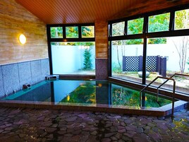Piscina interna com paredes de vidro transparente, piso de ladrilho de pedra e teto de madeira.
