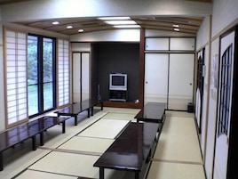 Um quarto japonês tradicional, com tatames, mesas baixas, portas deslizantes e uma televisão.