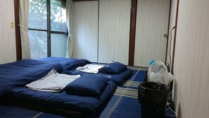 Quarto com cama, janela com cortinas, ventilador e lixeira.