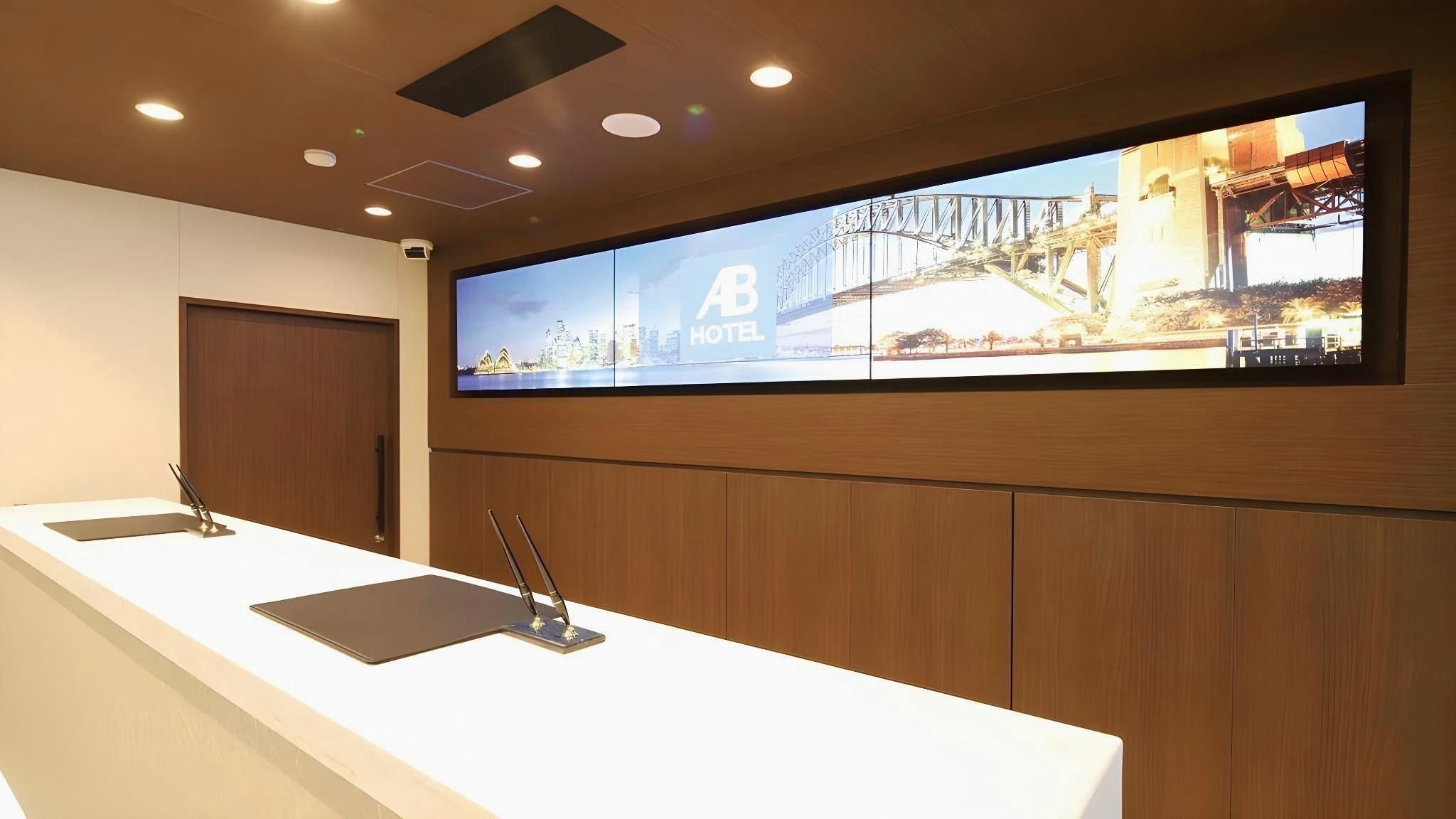 Bancada de recepção com uma grande tela digital exibindo uma paisagem urbana e o nome do hotel.