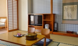 Um quarto em estilo japonês tradicional, com tatames, uma mesa de madeira baixa, uma televisão e um painel shoji.