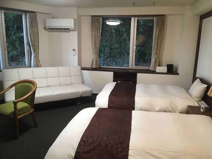 Quarto de hotel com duas camas, um sofá, uma poltrona, ar condicionado e uma janela com cortinas.