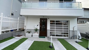 Um edifício residencial de dois andares com varanda, garagem com uma janela grande e cerca branca de piquete.
