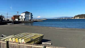 Uma praia com uma fileira de barcos, um edifício e uma montanha ao fundo.