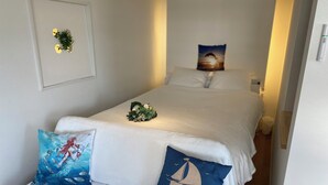 Quarto de hotel com duas camas, uma mesinha com uma planta e almofadas decorativas.