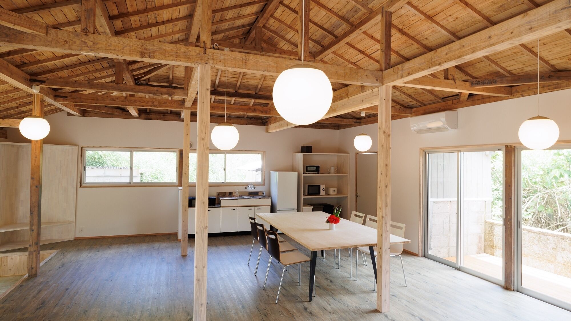 Uma cozinha ampla com vigas de madeira, área de jantar com mesa e cadeiras, e uma janela grande que proporciona luz natural.