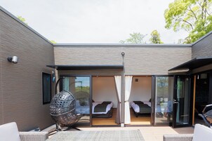 Um edifício moderno com fachada de tijolos, grandes portas de correr de vidro que dão para um quarto com duas camas e uma cadeira de vime do lado de fora.