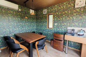 Uma sala de jantar com mesa e cadeiras de madeira, uma pequena cozinha com pia e chaleira, e uma janela com vista.