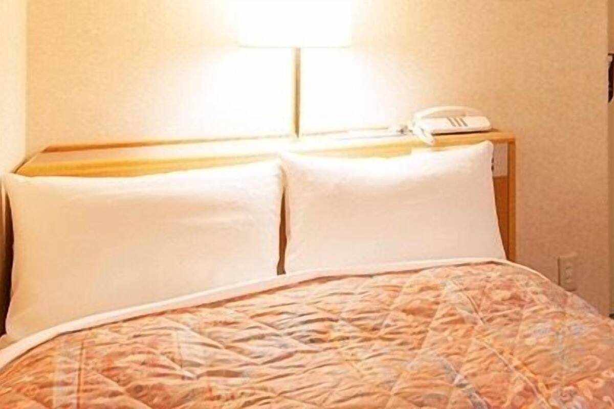 Quarto de hotel com cama, telefone ao lado e luminária na parede.