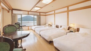 Quarto de hotel com uma janela grande, duas camas, uma mesa de jantar e cadeiras estofadas em verde.