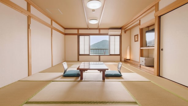 Um quarto japonês tradicional com tatames, uma mesa baixa e vista para uma montanha através de grandes janelas.