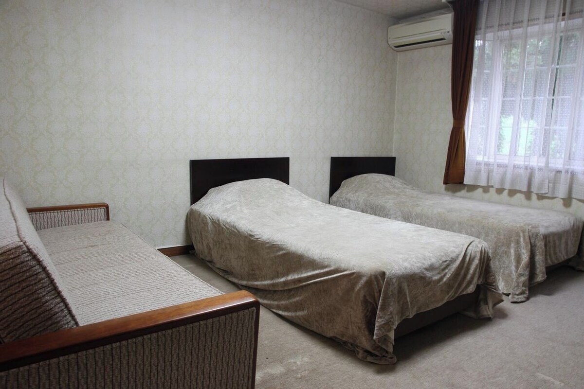 Quarto com duas camas de solteiro, uma escrivaninha de madeira e uma janela com cortinas.