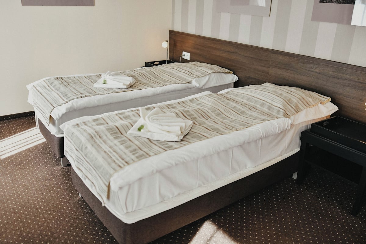 Quarto de hotel com duas camas de solteiro, cabeceira de madeira, mesa de cabeceira e piso coberto por carpete.