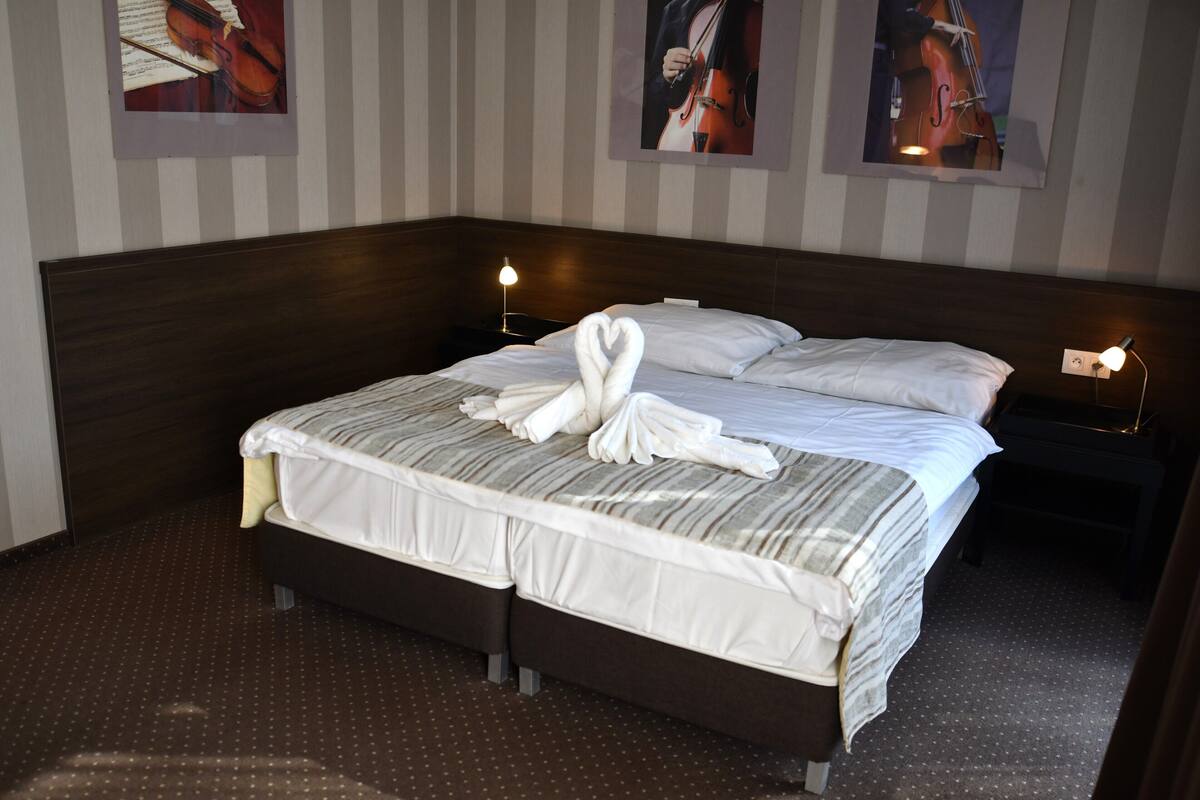 Quarto de hotel com cama de casal, duas mesas de cabeceira e obras de arte nas paredes retratando instrumentos de corda.