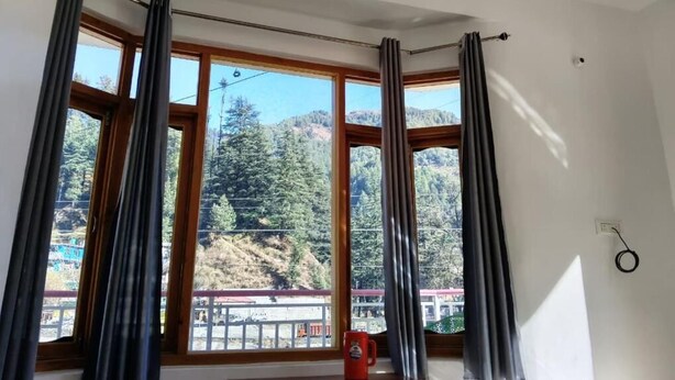 Quarto com grandes janelas, cortinas e vista para uma área arborizada.