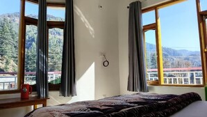 Quarto com uma cama grande, uma janela com cortinas e vista para uma paisagem montanhosa.