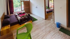 Um quarto amplo com cama, escrivaninha e cadeira. Há uma janela com cortinas, um ventilador de teto e uma porta que dá para outro cômodo.