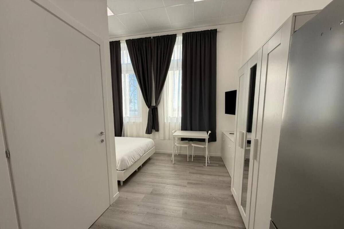 Quarto de hotel compacto com cama, escrivaninha e geladeira.