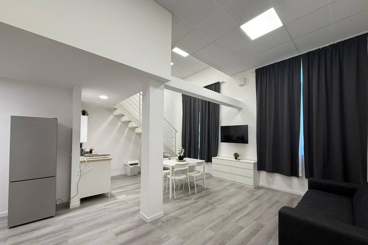 Um apartamento moderno com cozinha, área de refeições e sala de estar, apresentando uma escada, uma TV de tela plana e um sofá preto.