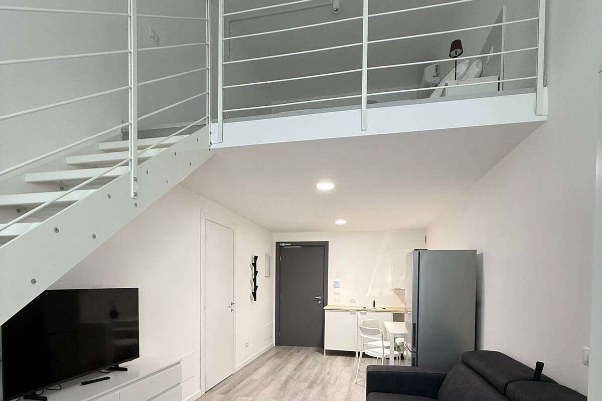 Um apartamento moderno com quarto no mezanino, sala de jantar e sala de estar com sofá.