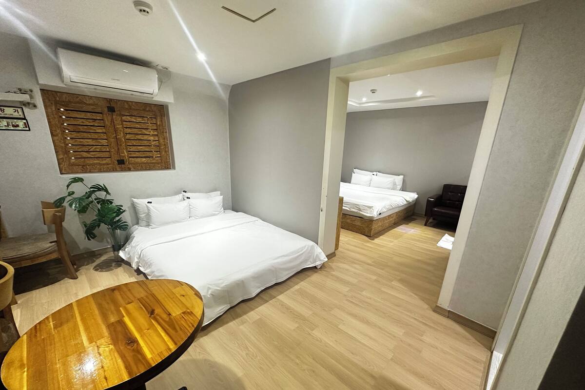 Quarto de hotel com cama, mesa de madeira, cadeira e planta em vaso.
