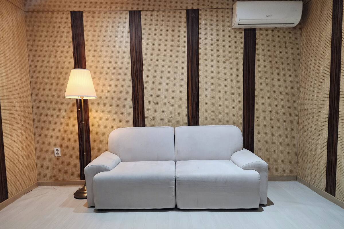 Um sofá branco em um quarto com uma parede perfurada, uma luminária e um ar condicionado.