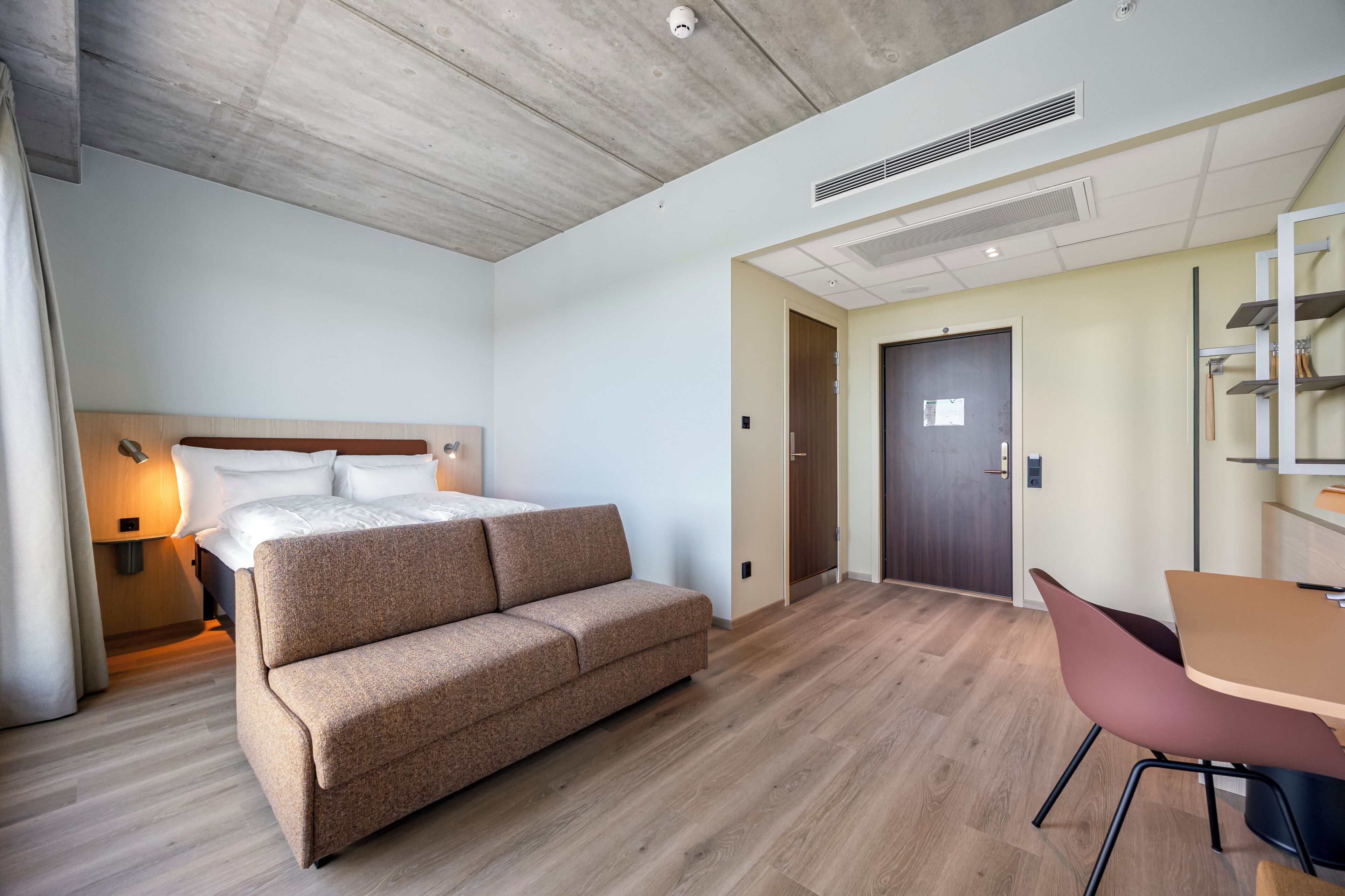 Quarto de hotel com cama, sofá, escrivaninha e cadeira.