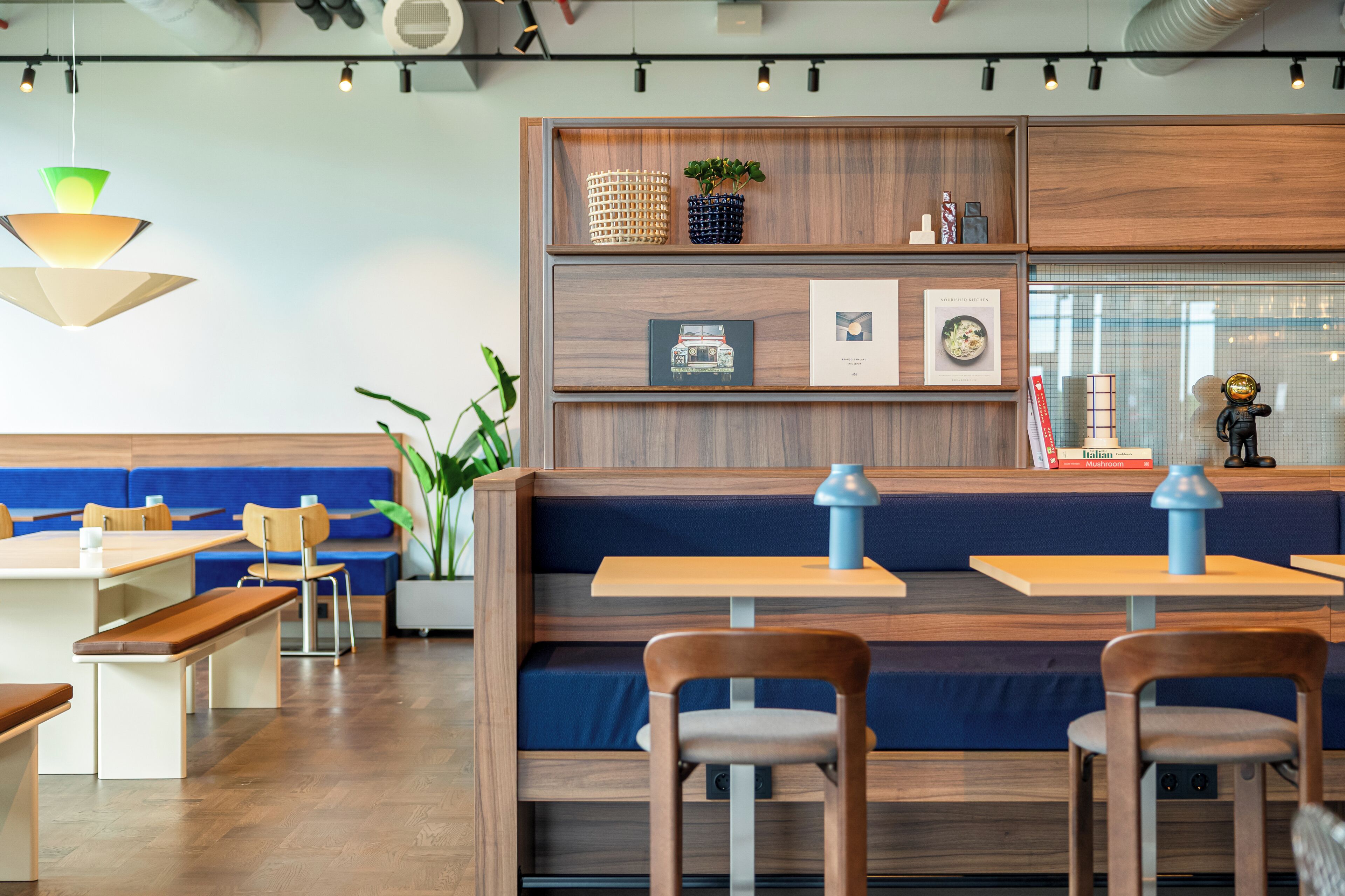 Restaurante moderno com mobiliário de madeira, assentos azuis e iluminação pendente.