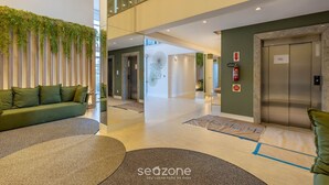 Um hall moderno com um sofá verde, um balcão de recepção, um elevador e uma parede com plantas verticais.