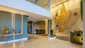 Um interior moderno com um balcão de recepção, sofás verdes e um grande painel decorativo.