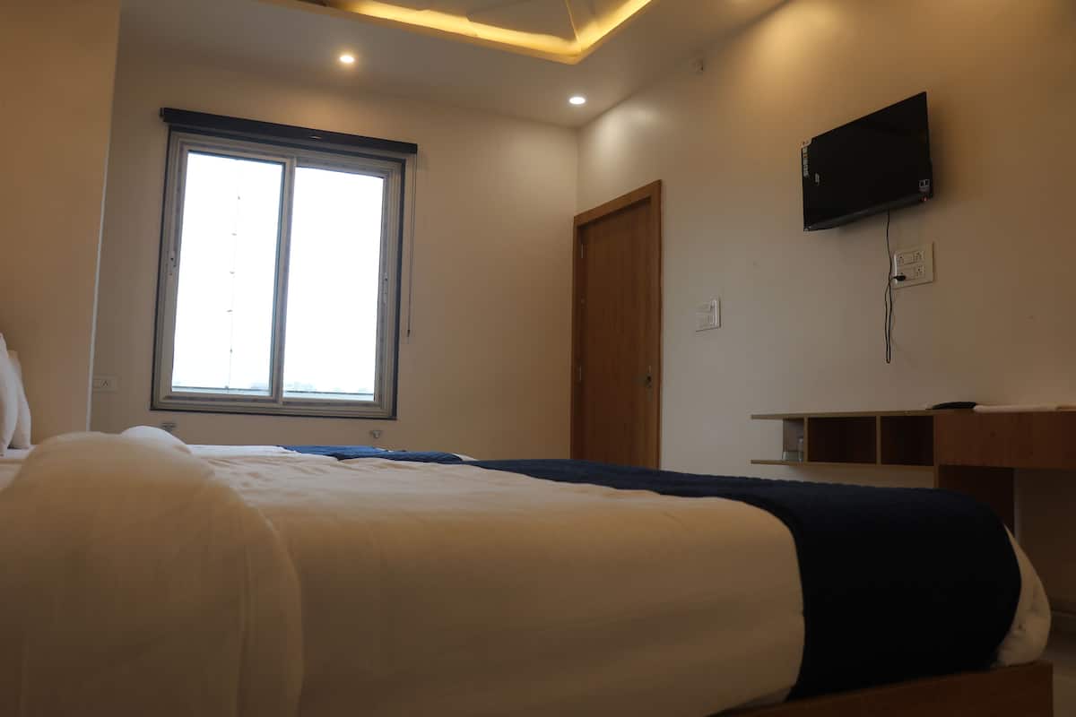 Quarto com cama, janela, porta, televisão na parede e mesa de cabeceira.