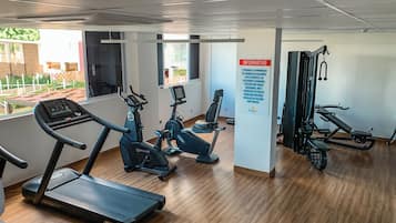 Academia com diversos equipamentos de exercício, incluindo esteiras e bicicletas ergométricas, e um aviso com instruções de segurança.