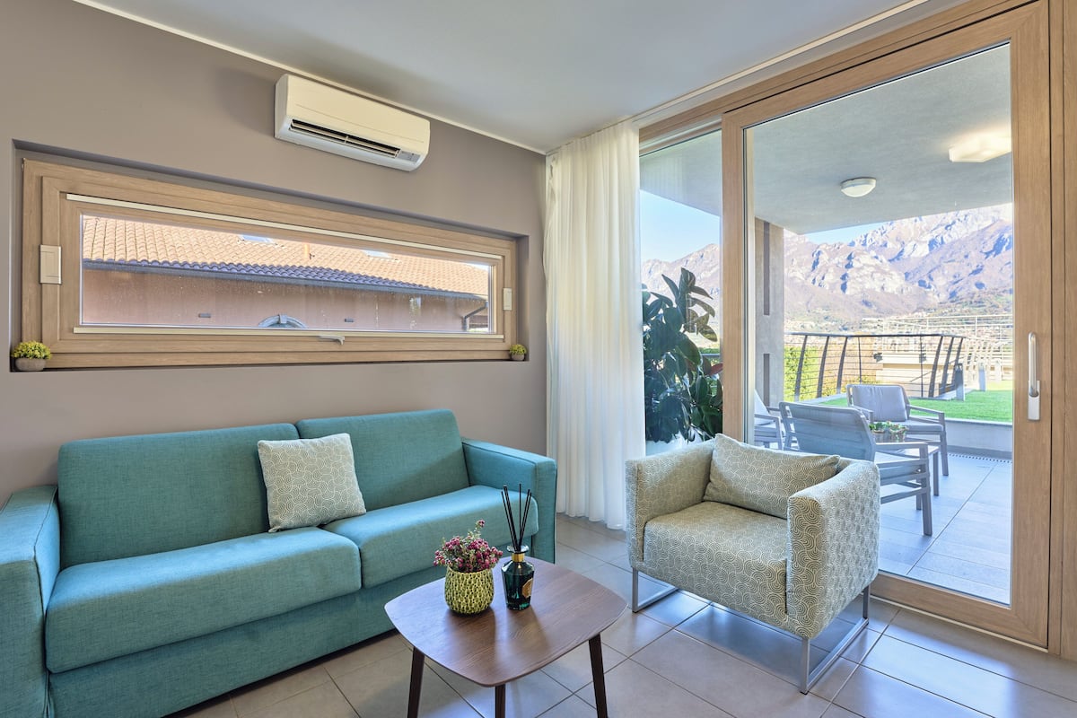 Sala de estar com sofá, poltrona, mesa de centro e janela com vista para uma varanda.